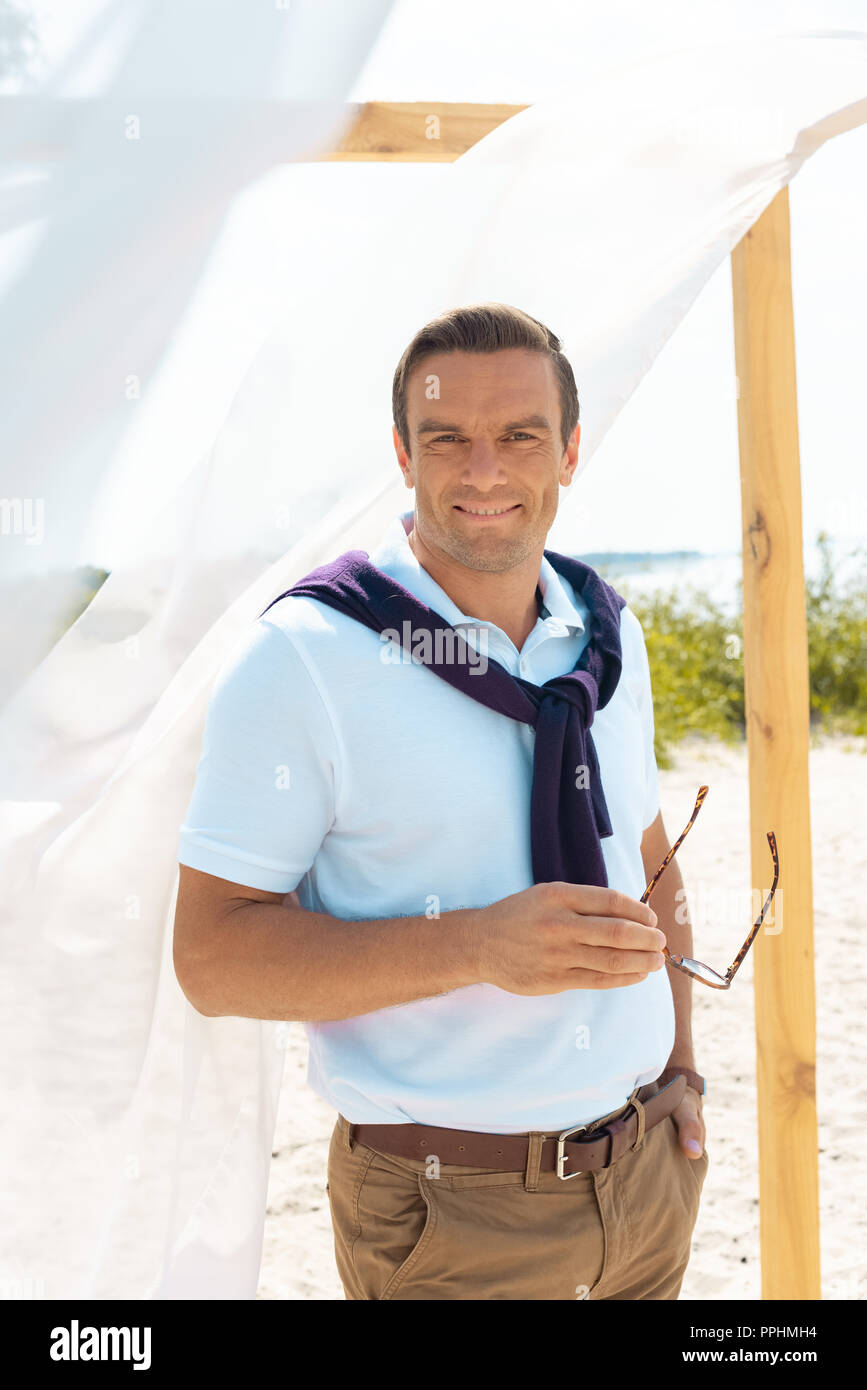portrait of stylish smiling man with eyeglasses standing at decoration ...