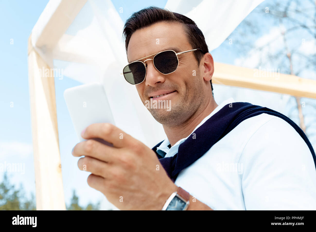 portrait of handsome man in sunglasses using smartphone with blue ...