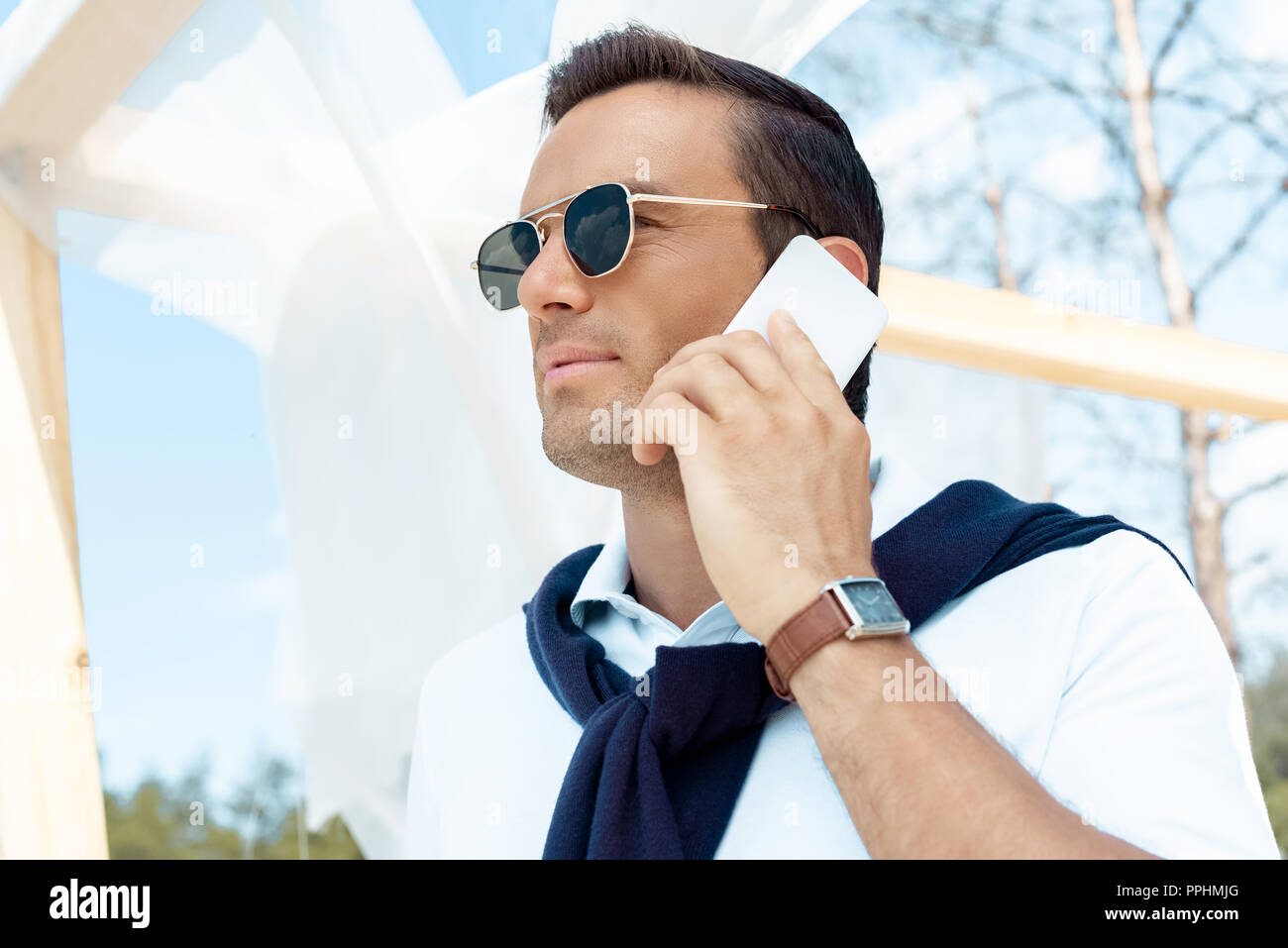 portrait of handsome man in sunglasses talking on smartphone with blue ...