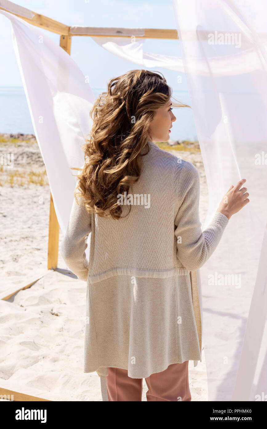 back view of woman standing near wooden decoration with white curtain ...