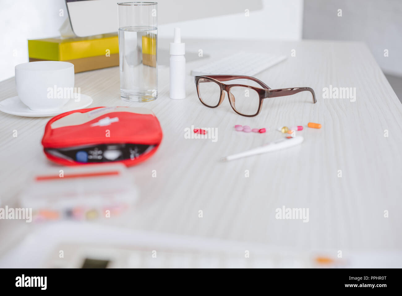 first aid kit, pills, glasses and glass of water on table in office ...
