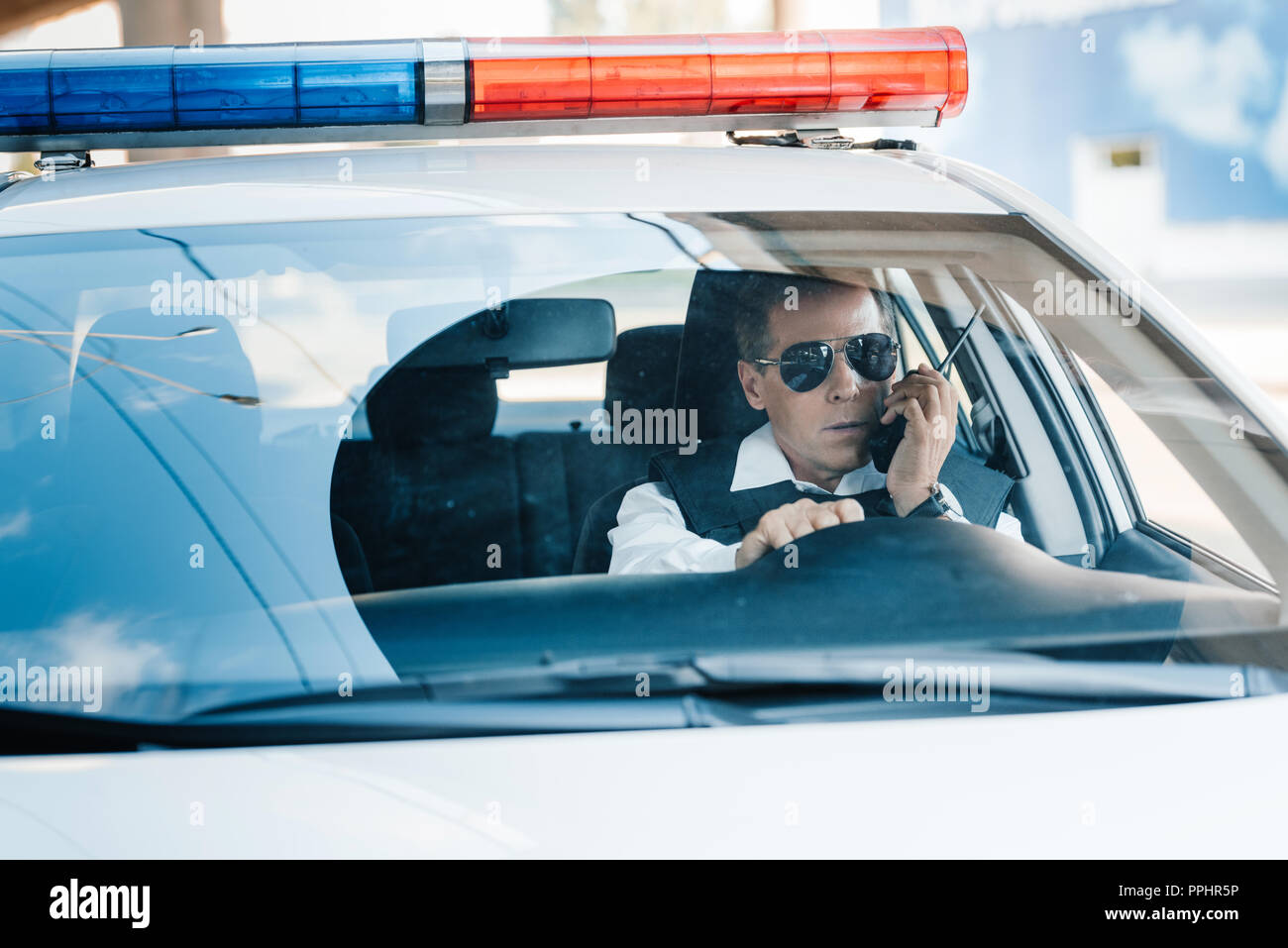 serious middle aged policeman in sunglasses talking on radio set in car ...