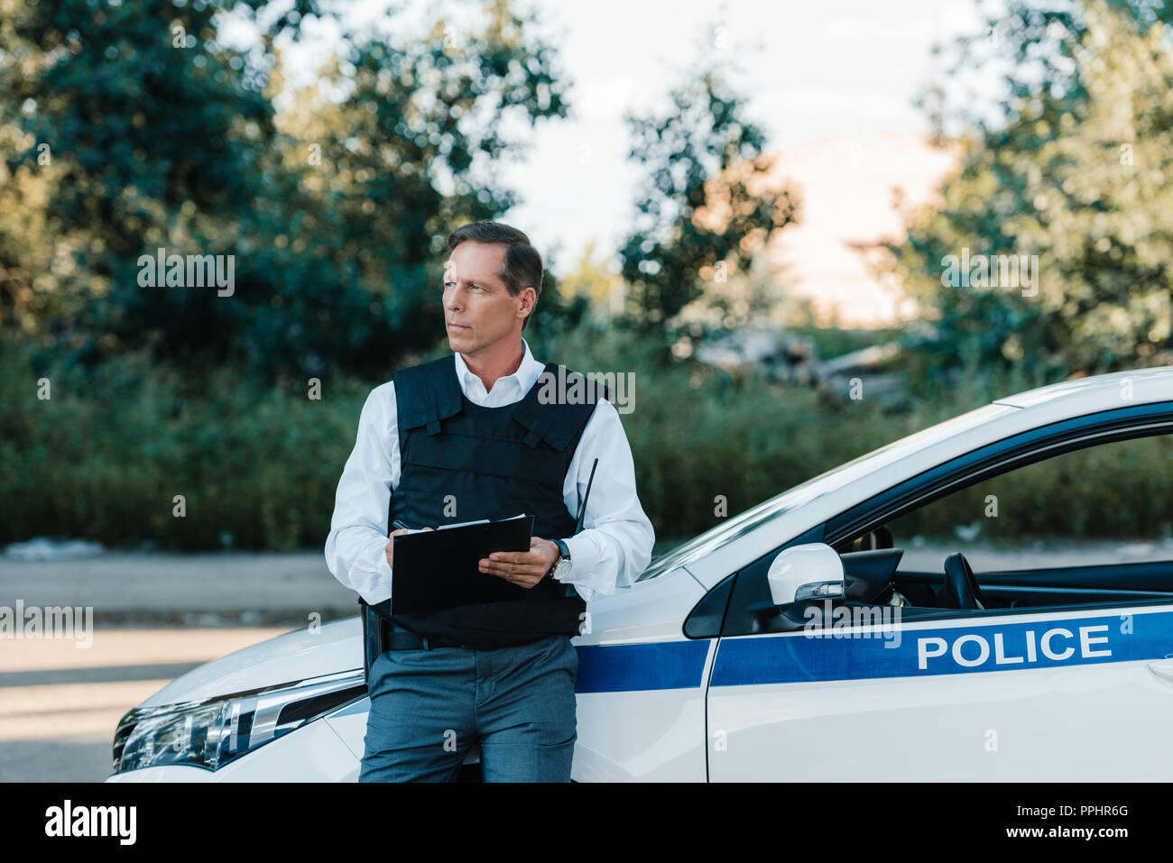 middle aged male police officer in bulletproof vest writing in ...