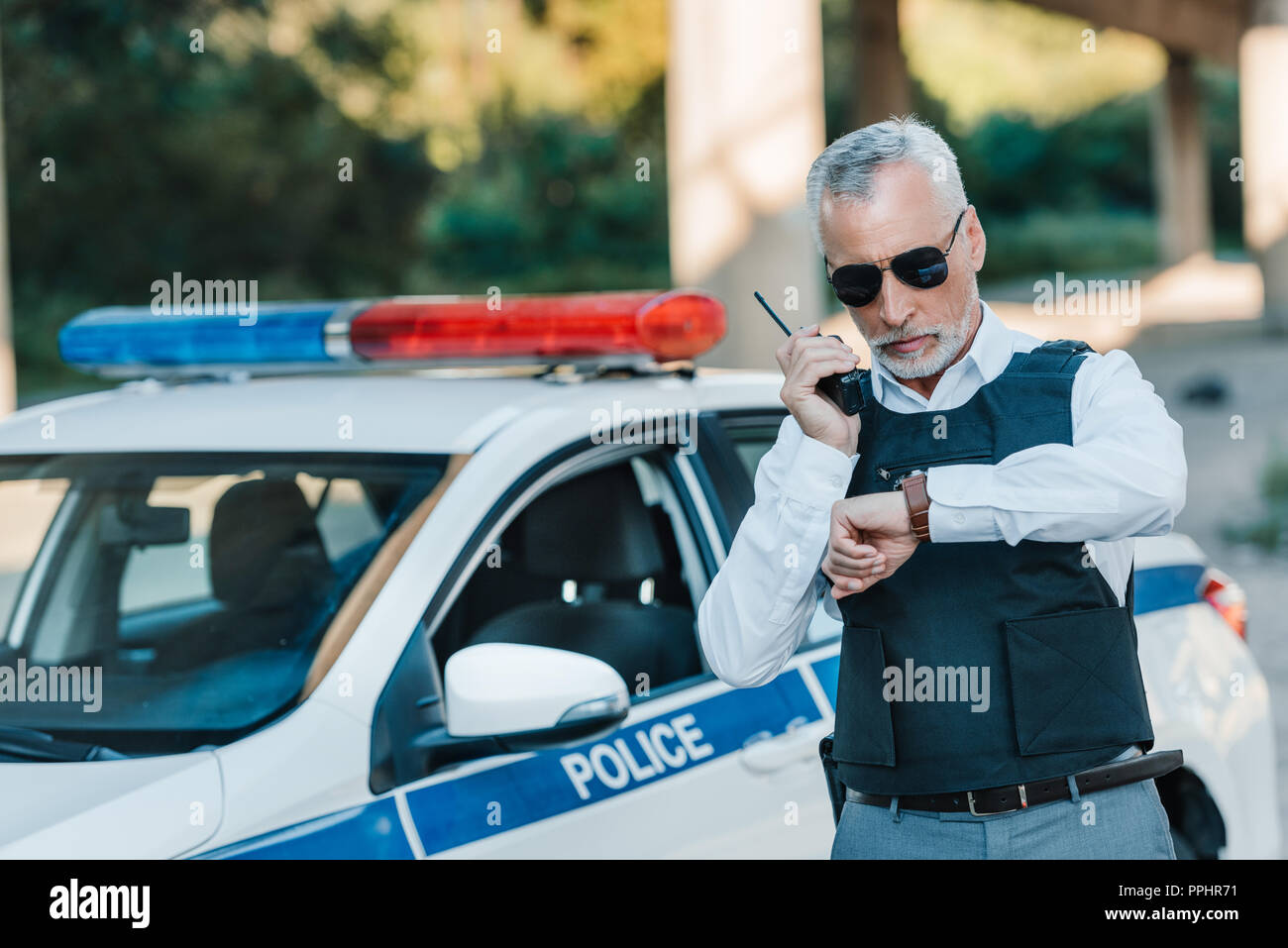 middle aged policeman in bulletproof vest and sunglasses checking ...
