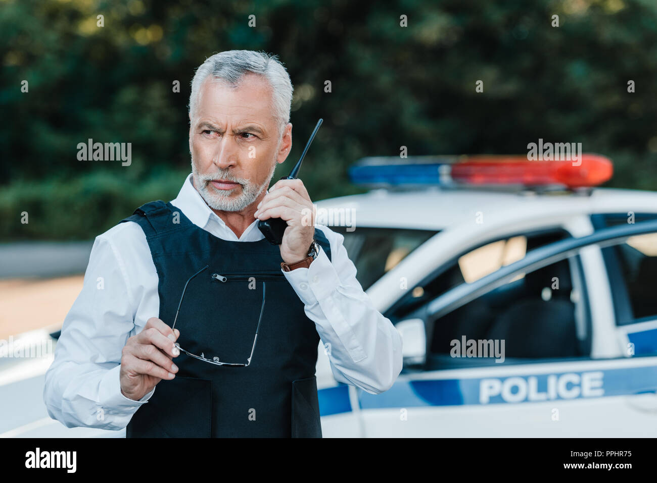 serious middle aged policeman in bulletproof vest talking on radio set ...