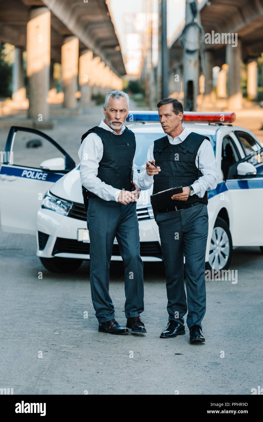 male police officer with clipboard pointing by finger to colleague ...