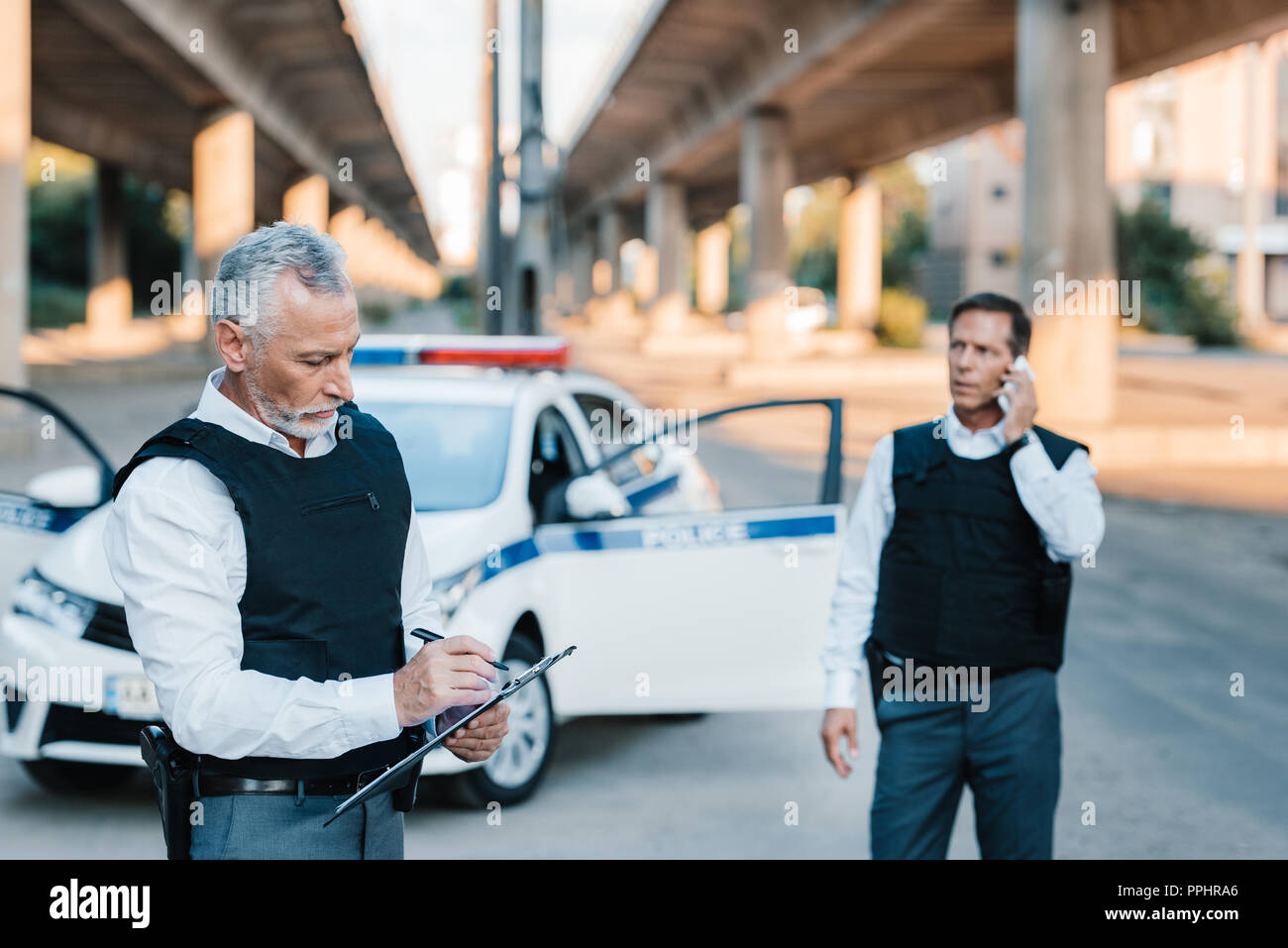 middle aged police officer writing in clipboard while his colleague ...