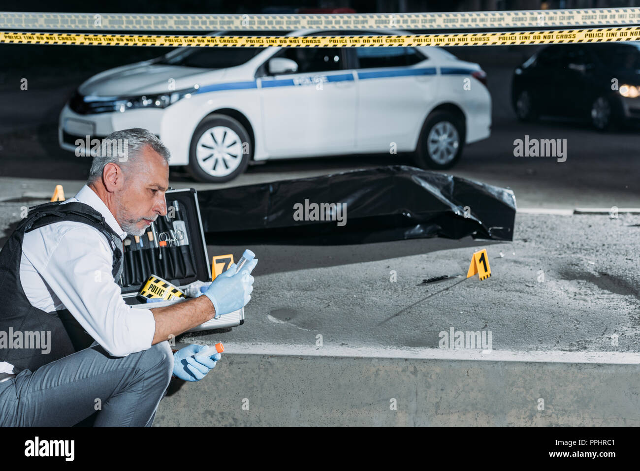 side view of policeman collecting evidence near cross line at crime ...