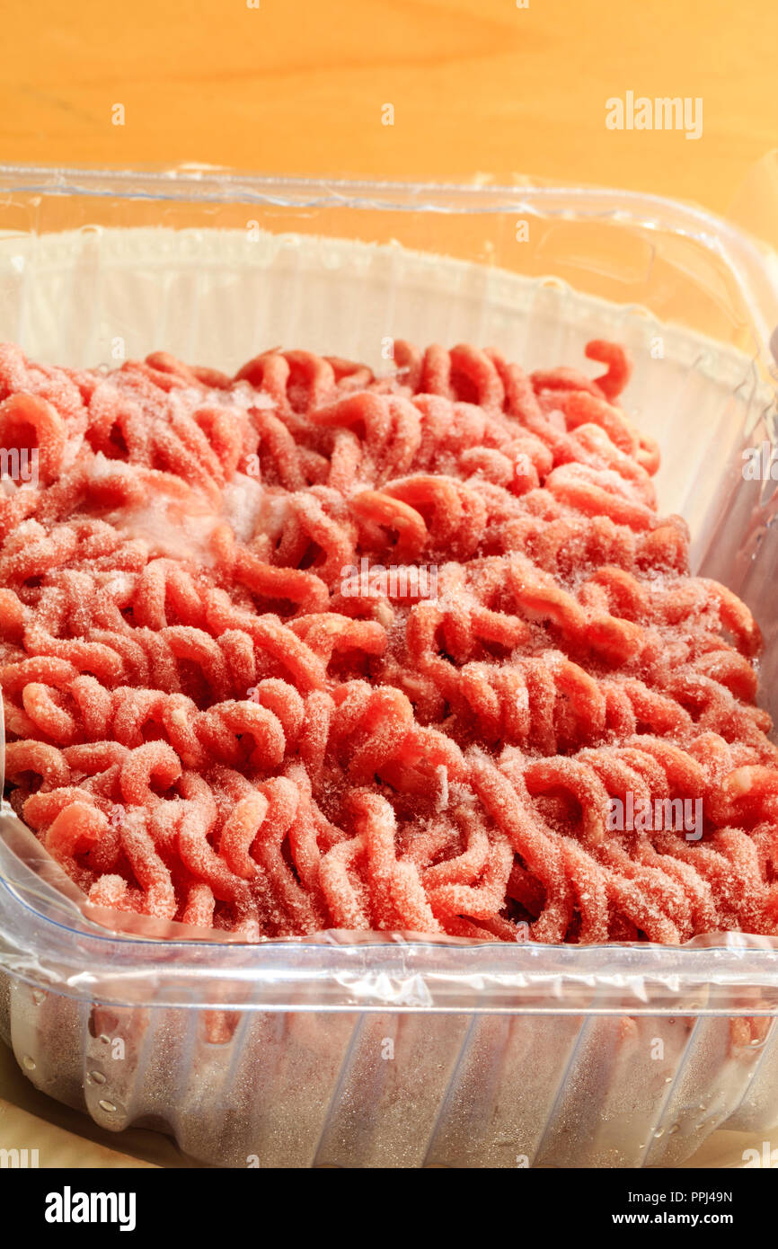Frozen beef mincemeat in white plastic container defrosting in sunlight ...