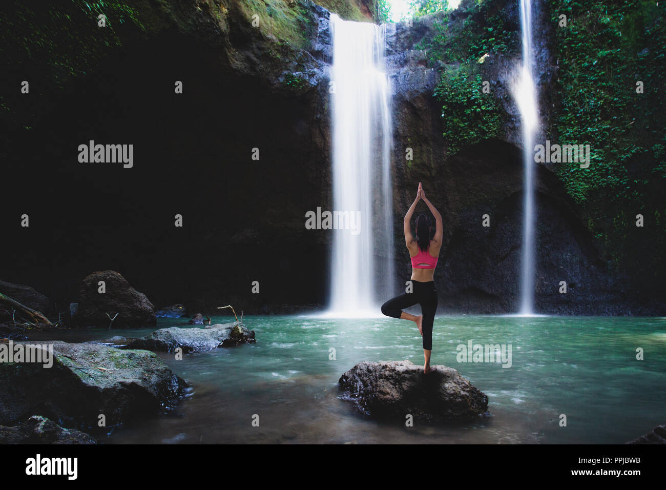 young women meditate while doing yoga at the waterfall in the forest ...