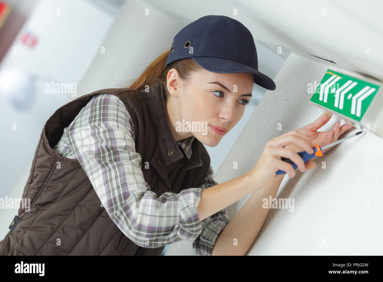 female technician fitting a fire exit sign Stock Photo - Alamy