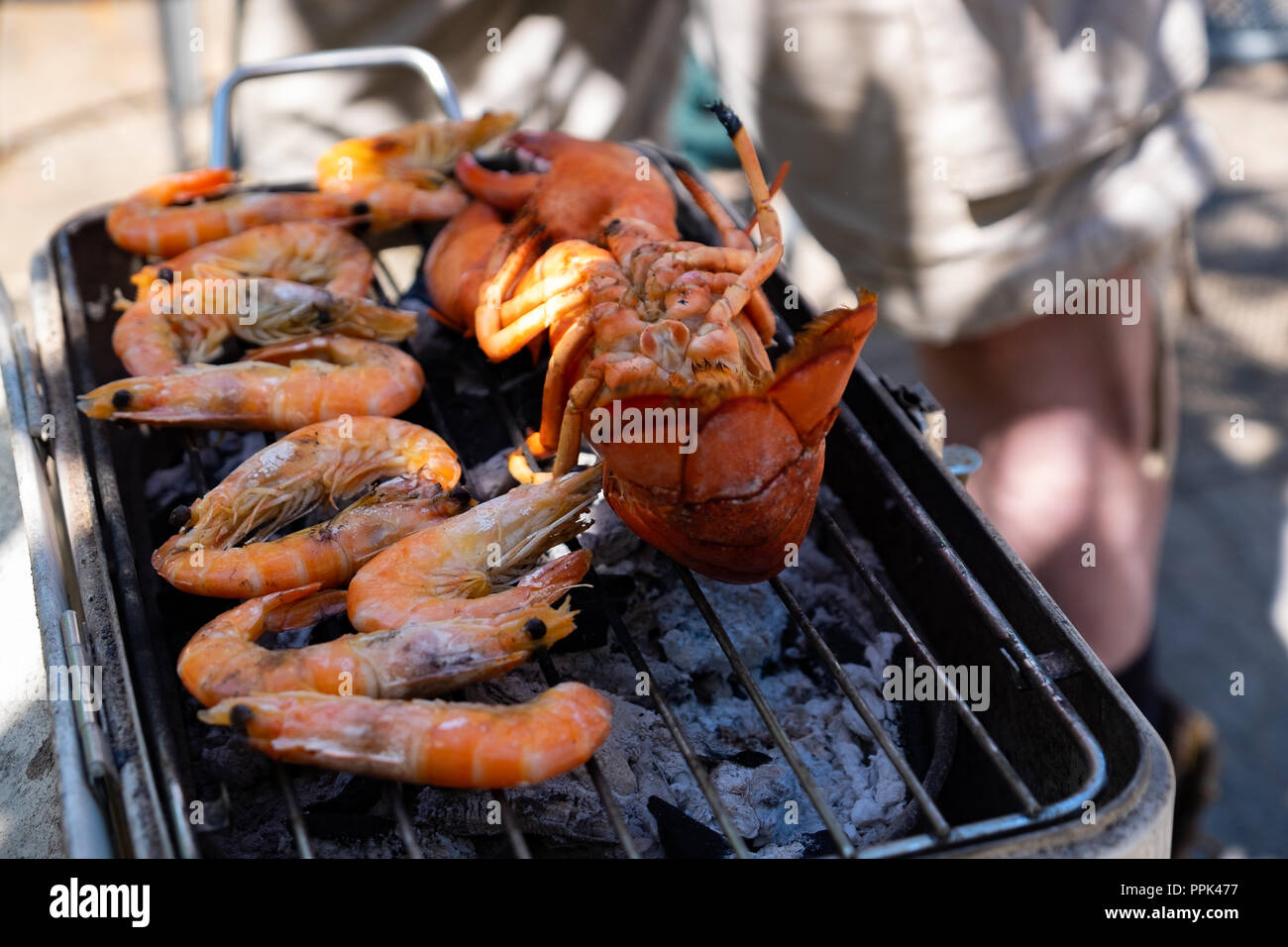 Man BBQing king prawns and lobster tail on small BBQ on the patio in ...