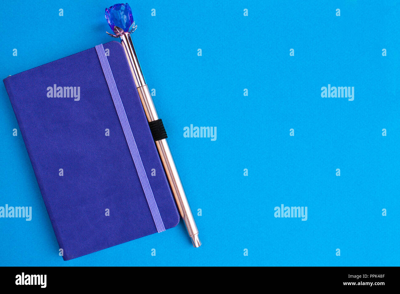 Purple notebook with pen on a blue background Stock Photo - Alamy