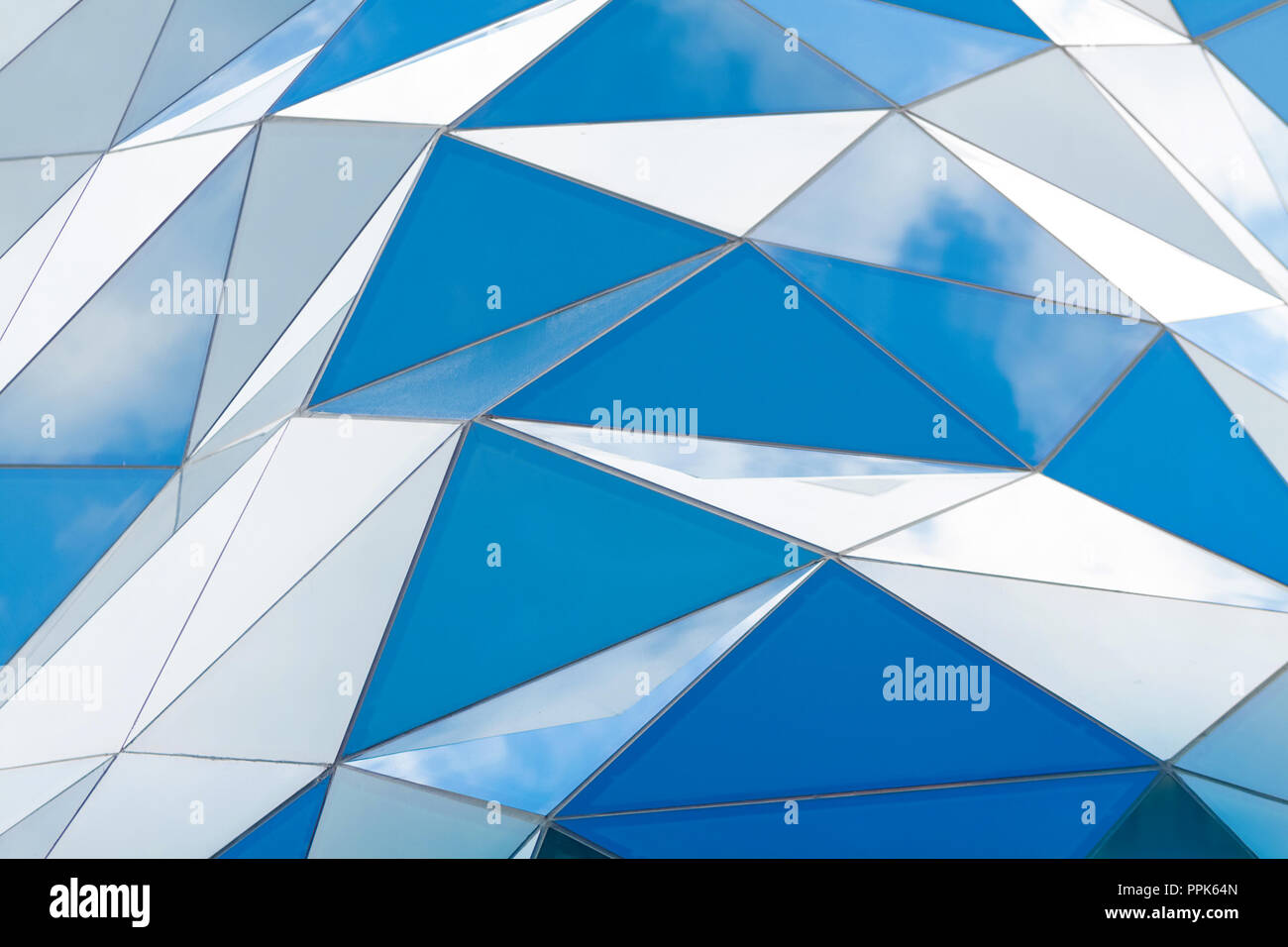 Polygonal triangle glass facade of modern building. Cloudy sky reflects ...