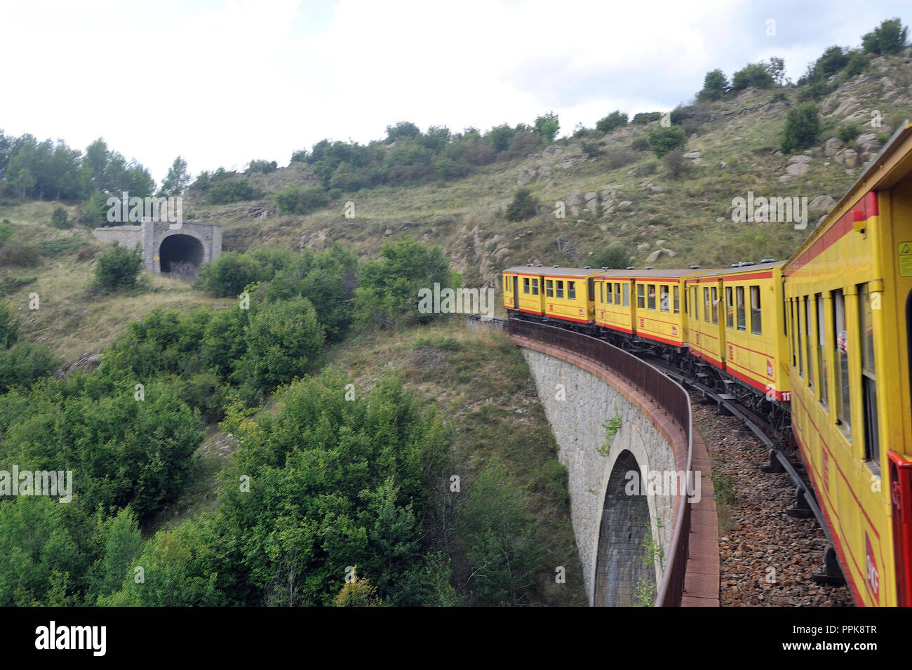 The small yellow train of the Pyrenees crossing a beautiful mountain ...