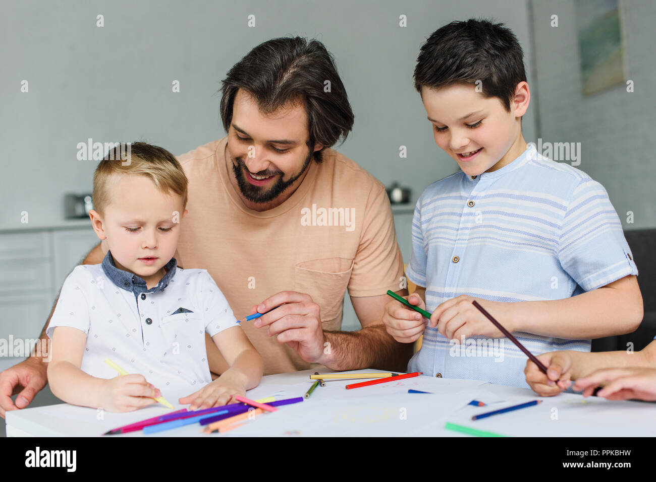 portrait of father helping sons draw pictures with colorful pencils at ...