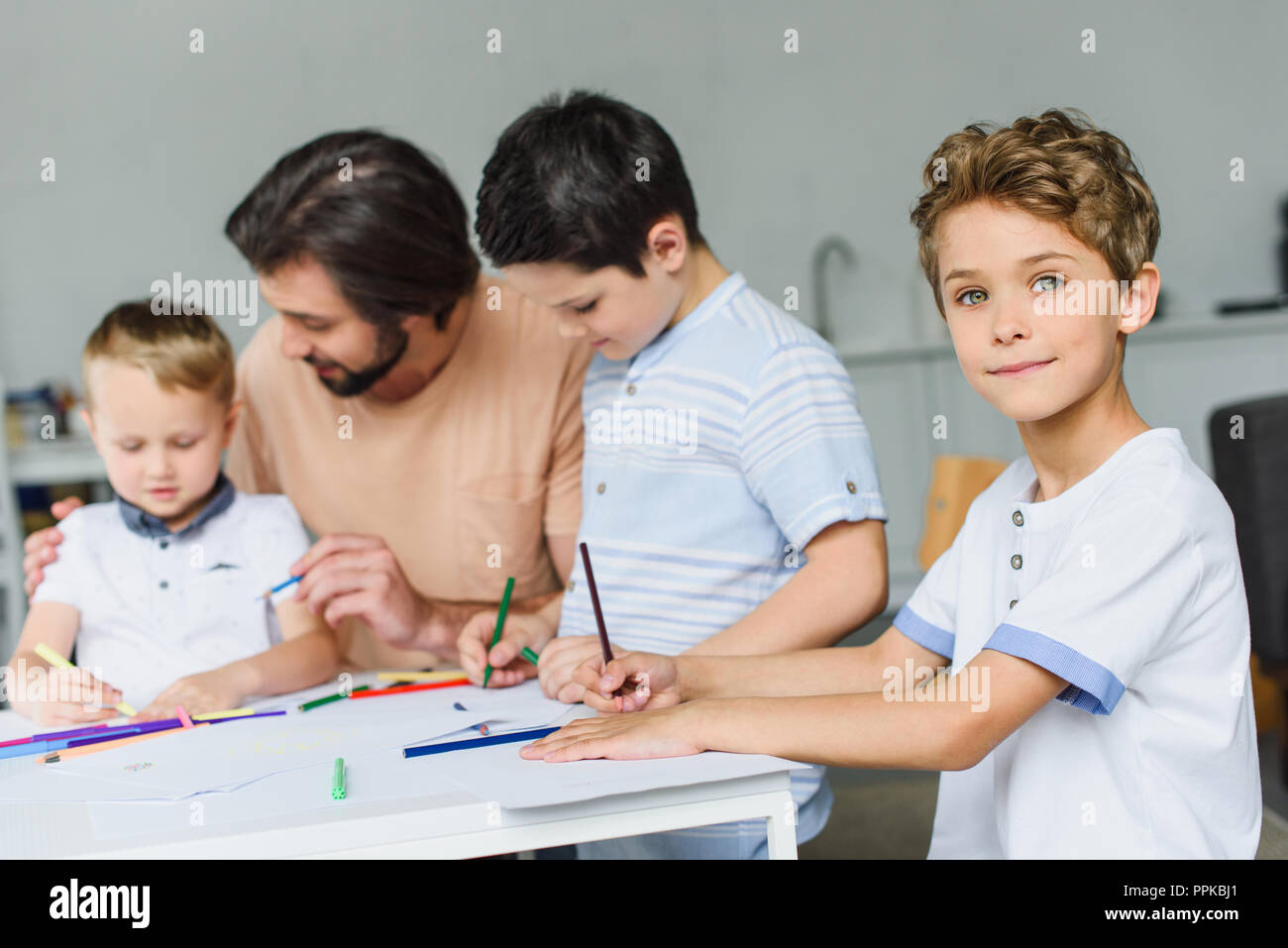 selective focus of father helping sons draw pictures with colorful ...