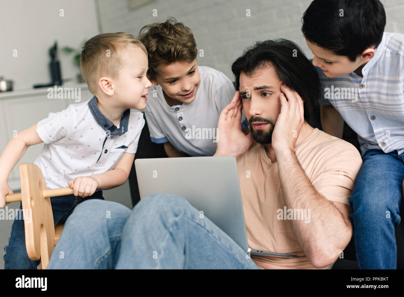 portrait of stressed father with laptop and little kids around at home ...