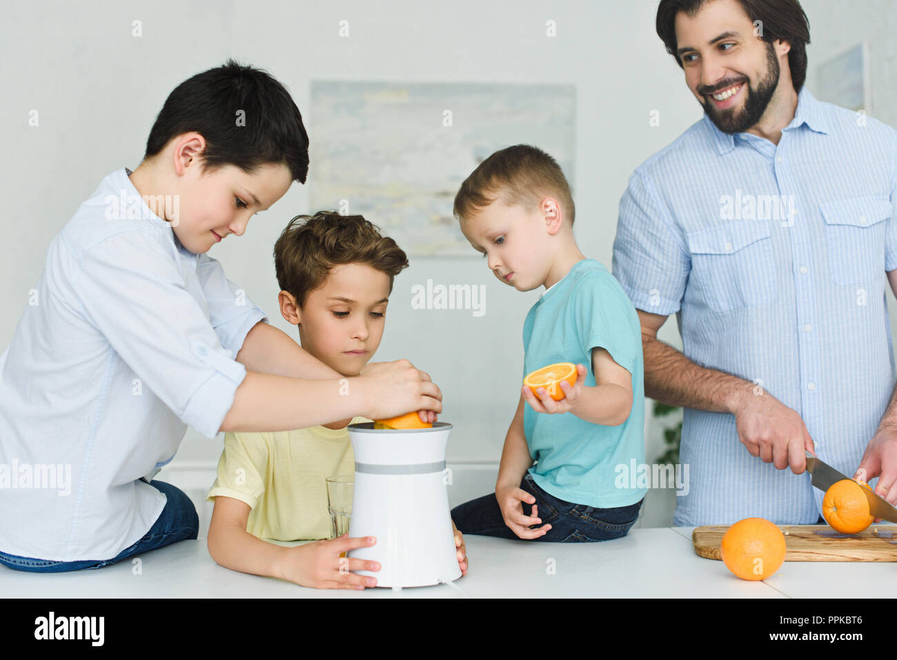 portrait of father and sons making fresh orange juice in kitchen at ...