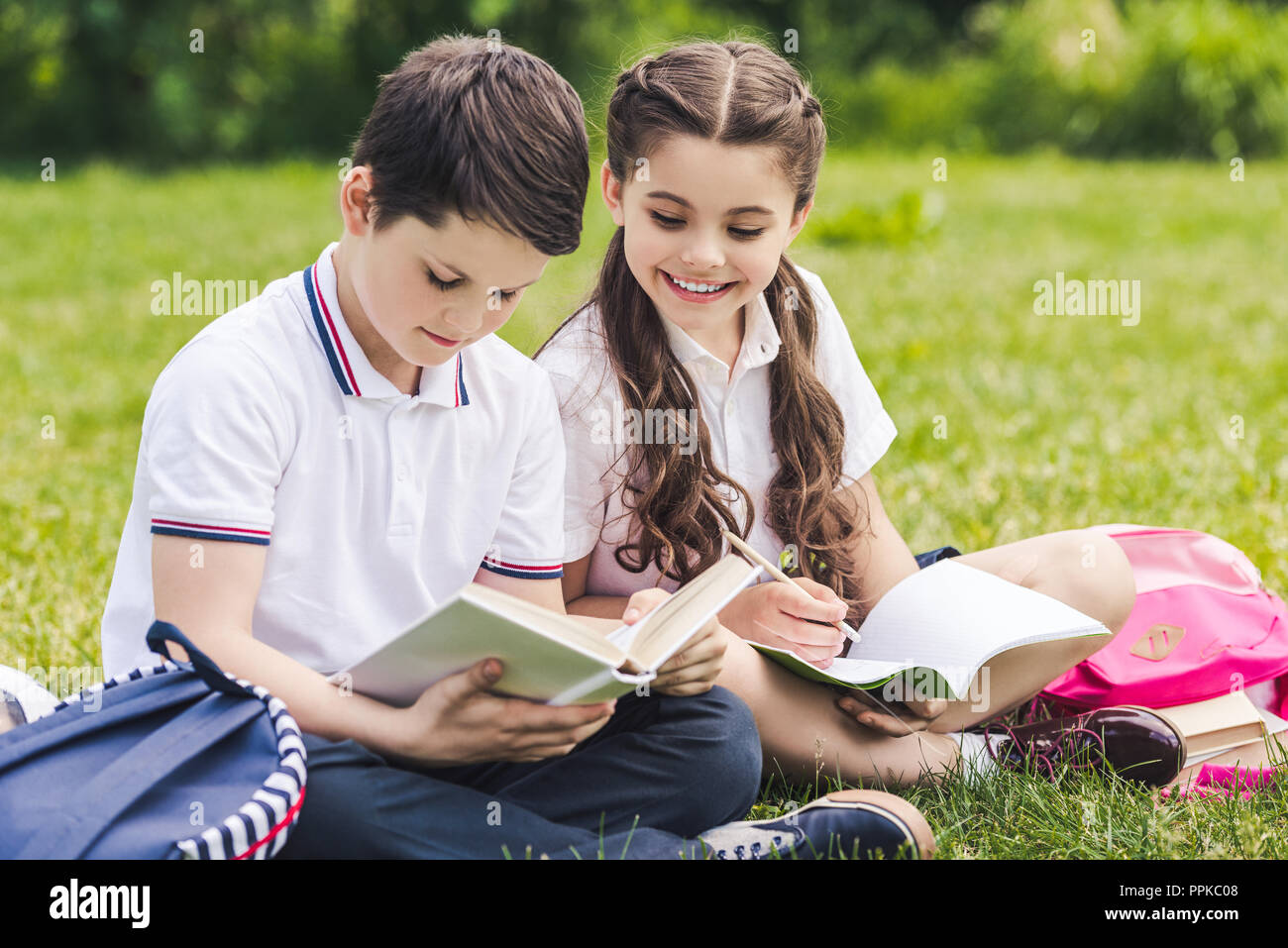 cute schoolchildren doing homework together while sitting on grass in ...
