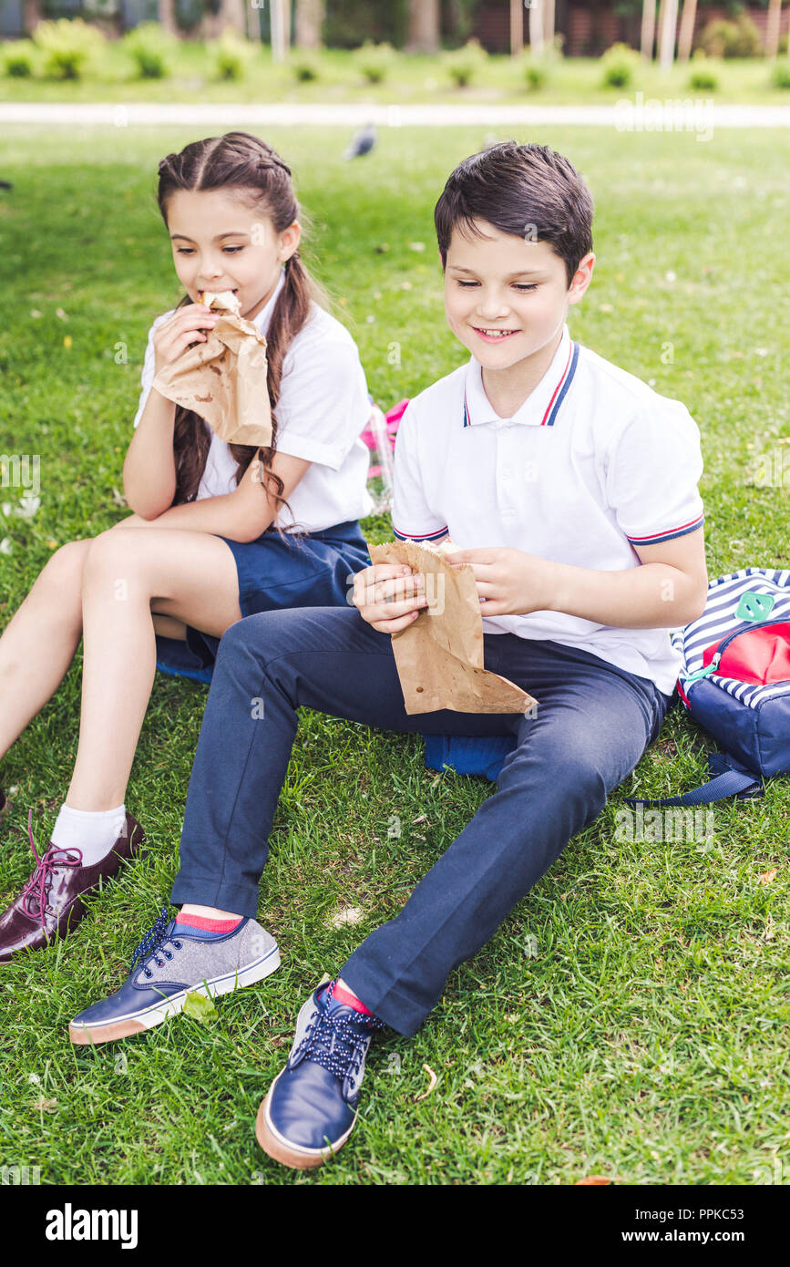 adorable schoolchildren sitting on grass and eating sandwiches Stock ...