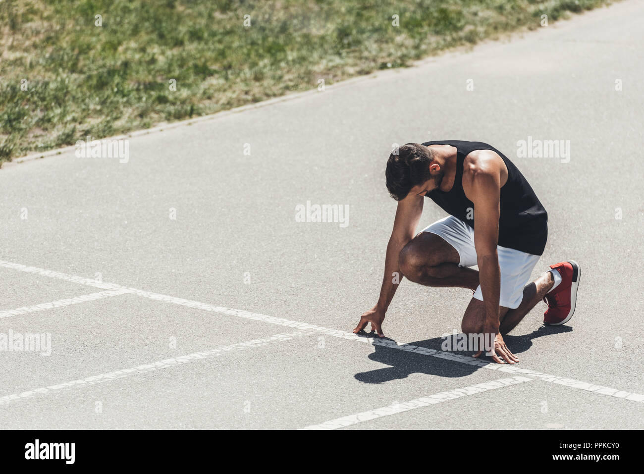 young sportsman in starting position on running track at sport ...