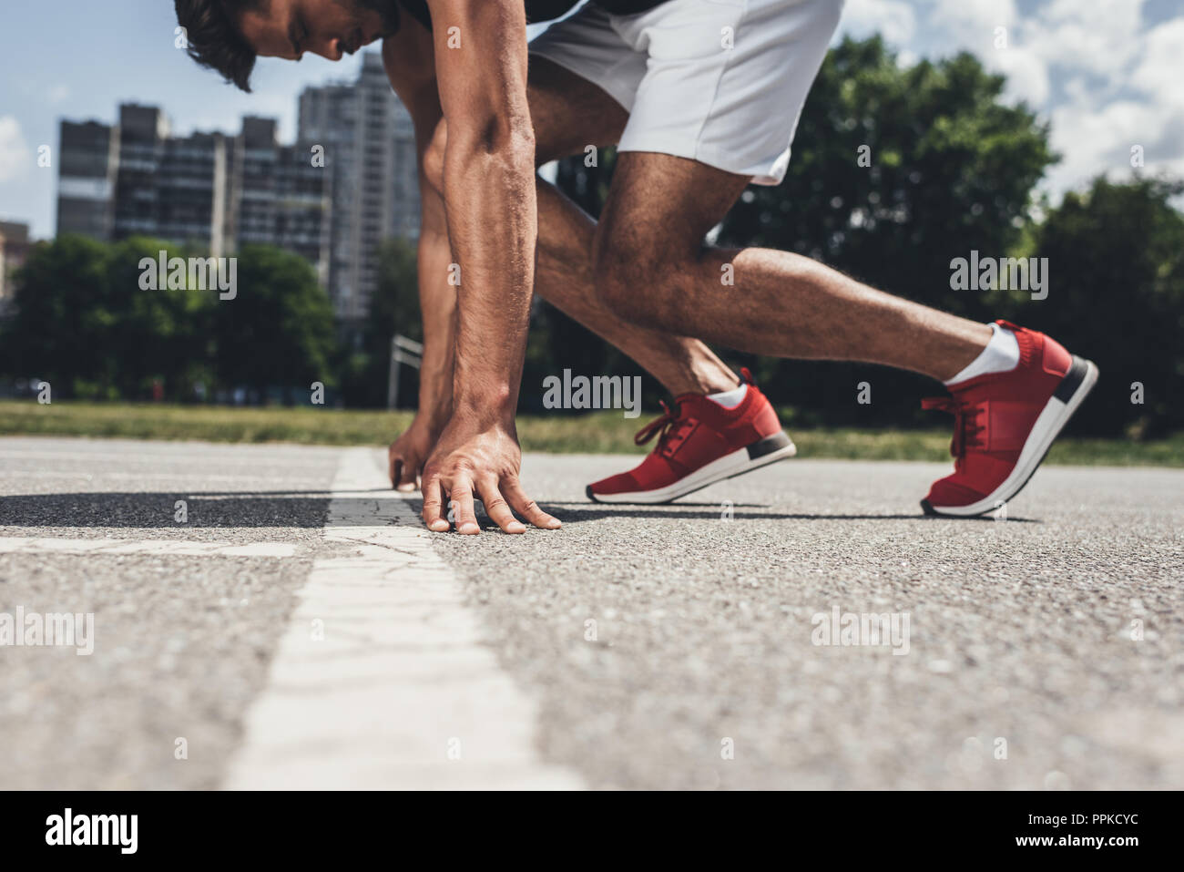 partial view of male sprinter in starting position on running track ...