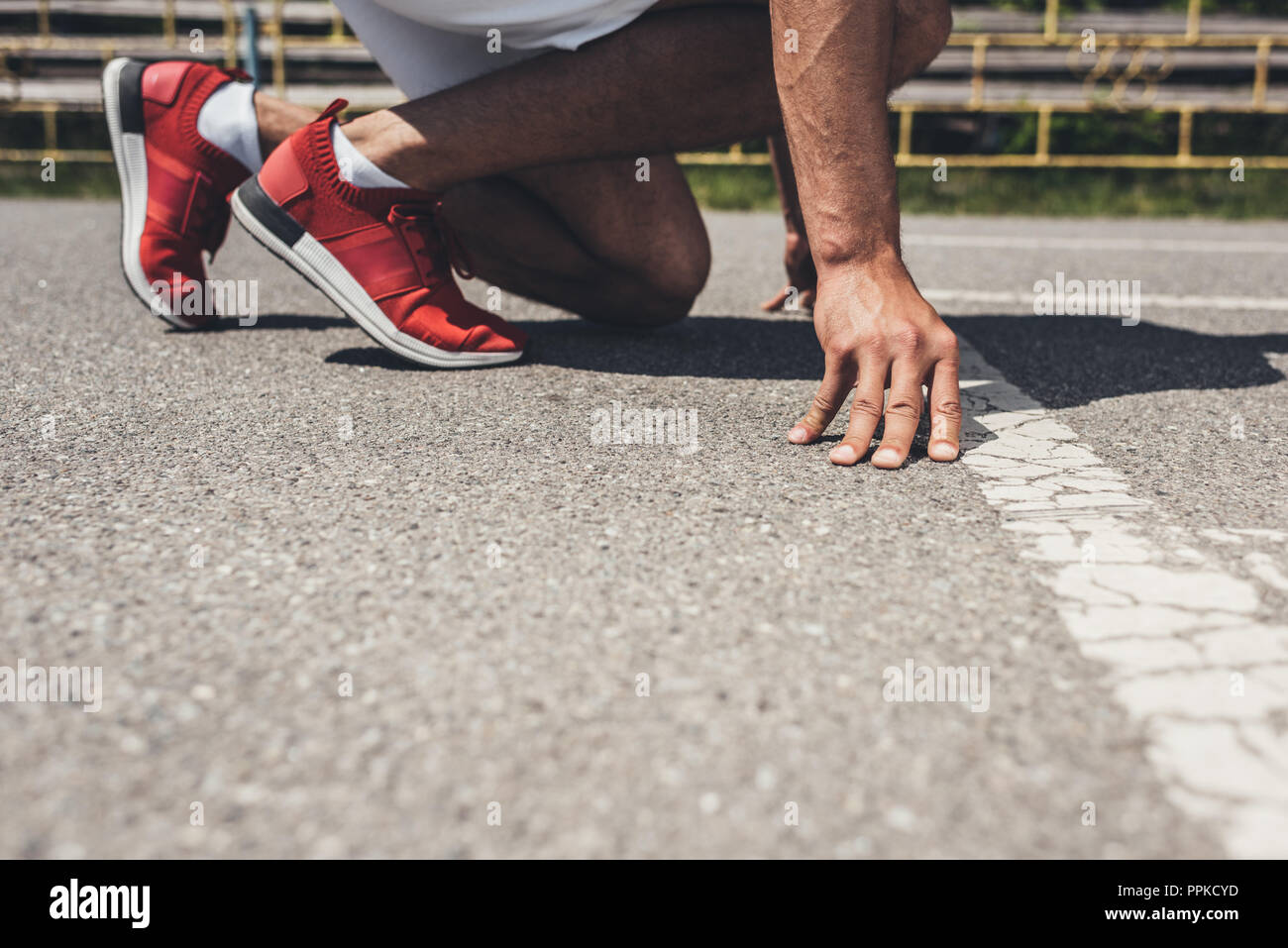 cropped image of male sprinter in starting position on running track ...