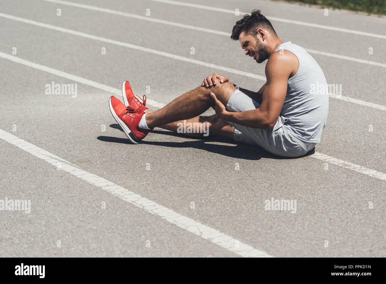 young runner with leg injury sitting on floor of running track Stock ...