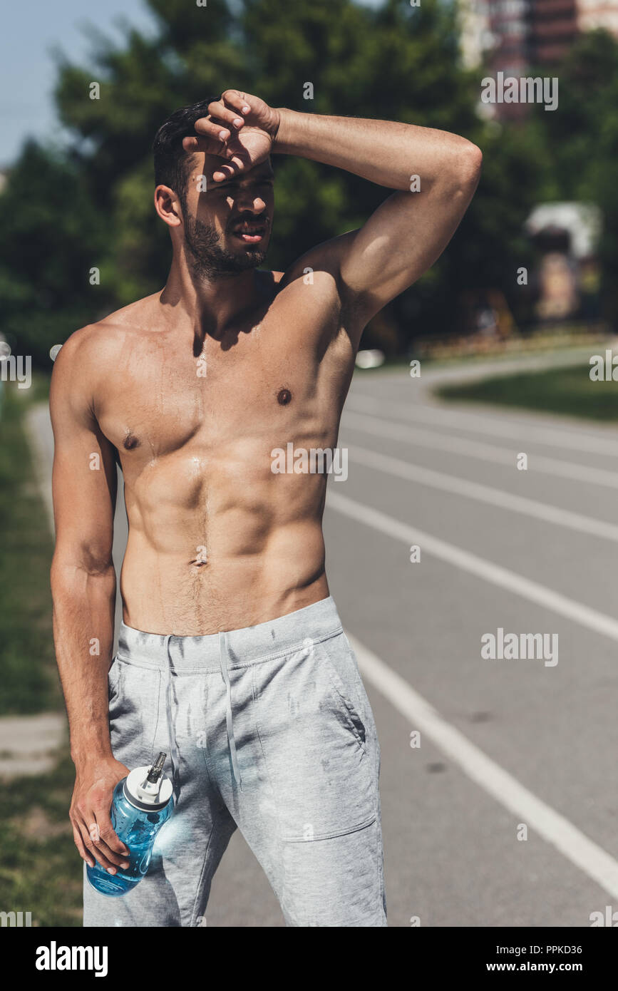 sweat shirtless young man standing on running track after workout and ...