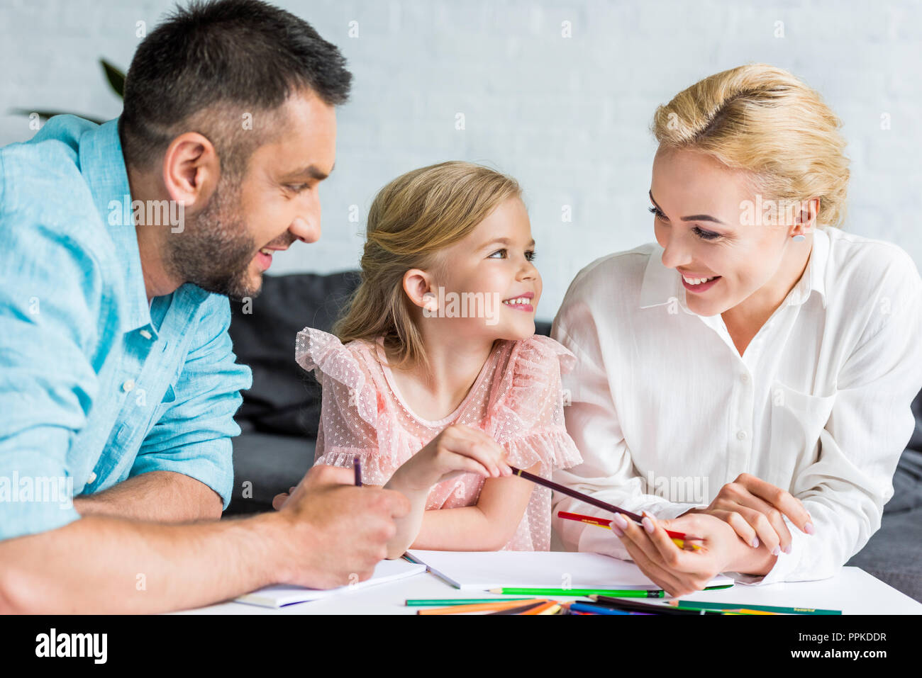 happy parents and cute little daughter drawing with colored pencils ...