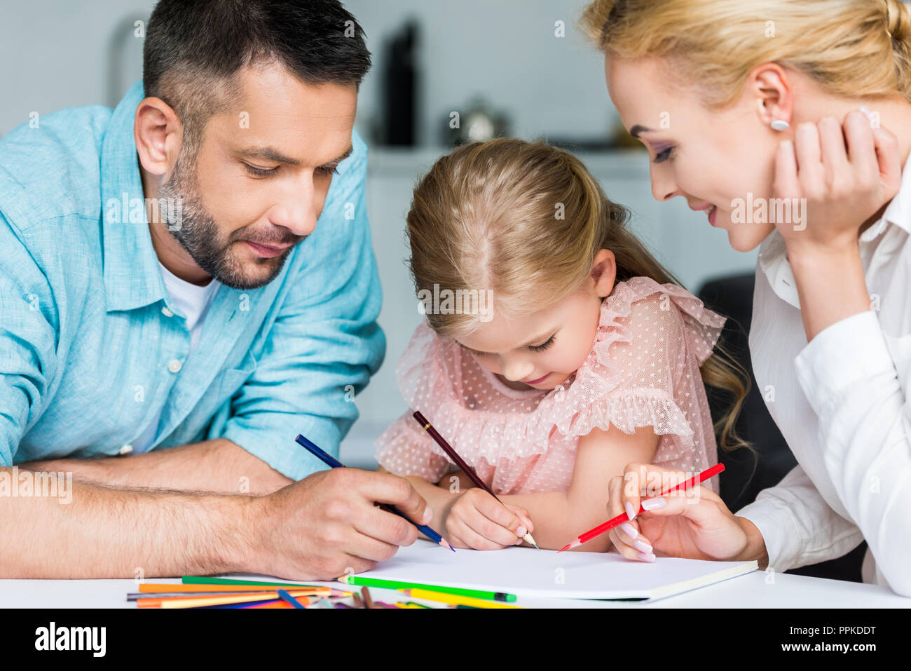 parents with cute little daughter drawing with colored pencils together ...