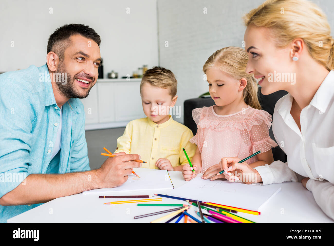 happy parents with two little kids drawing with colored pencils at home ...