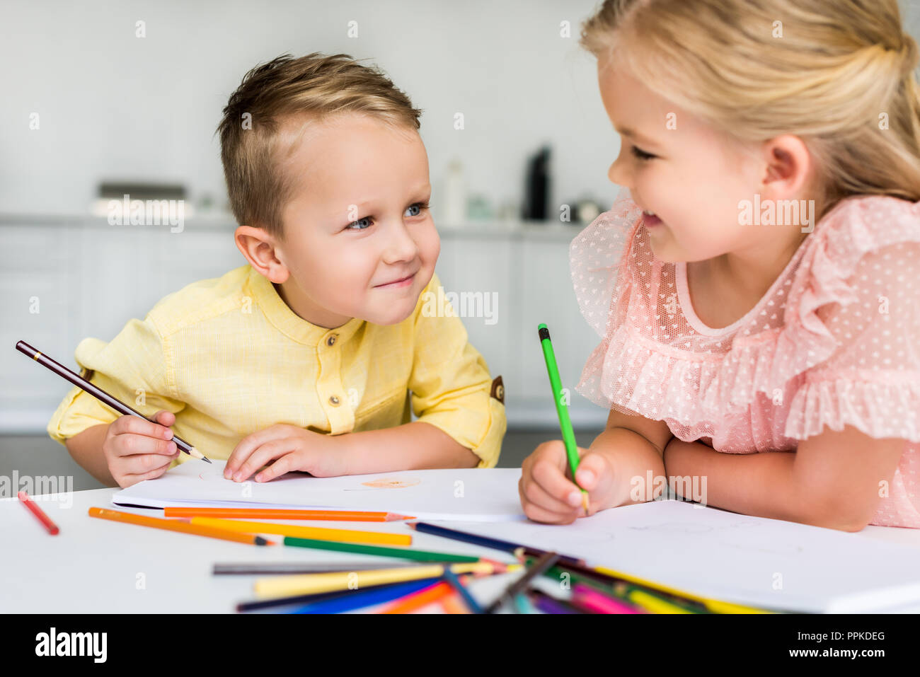adorable kids smiling each other while drawing with colored pencils ...