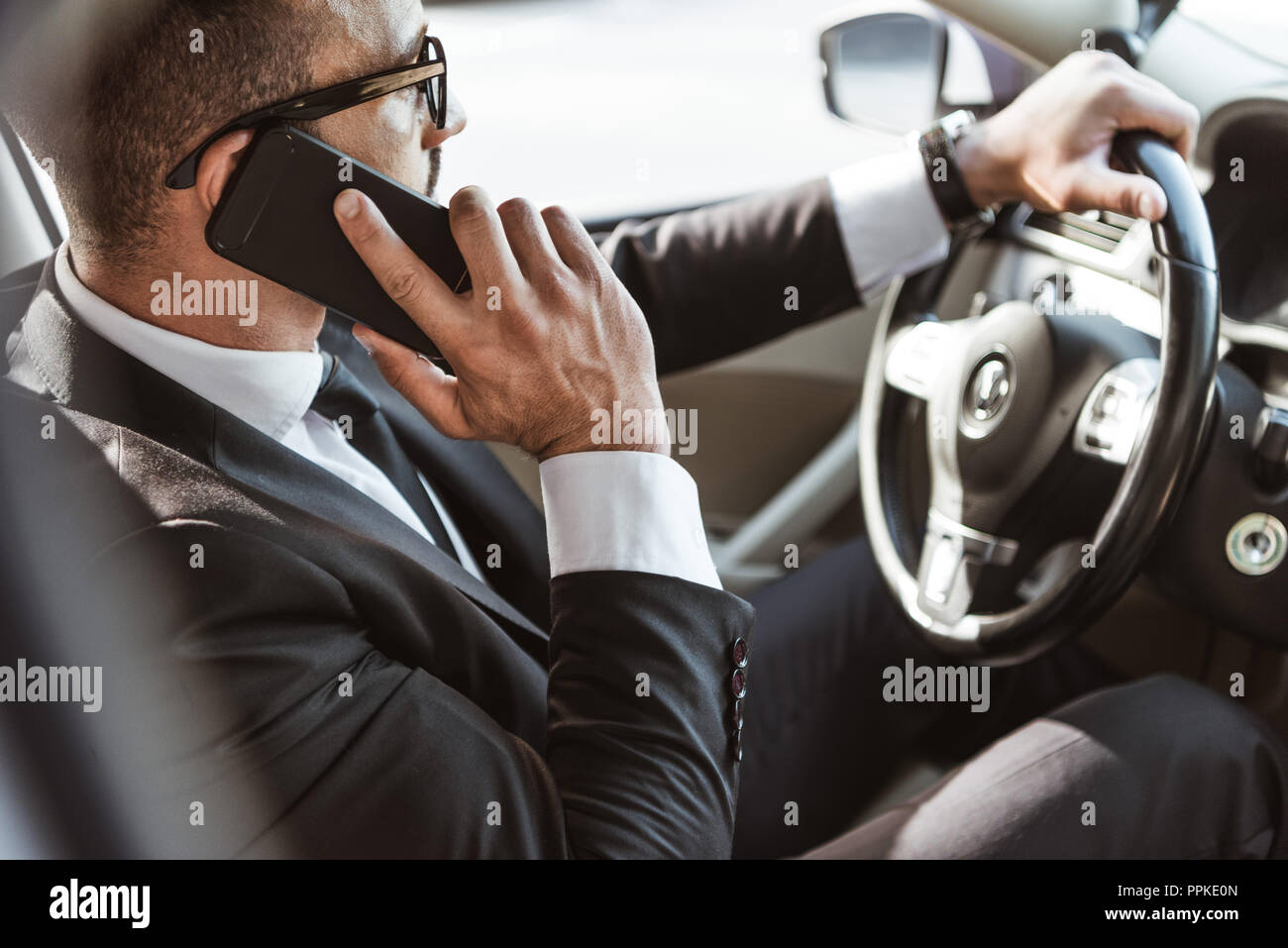 side view of handsome driver in suit driving car and talking by ...