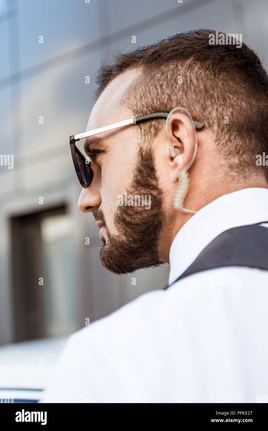 side view of handsome security guard with security earpiece on street ...