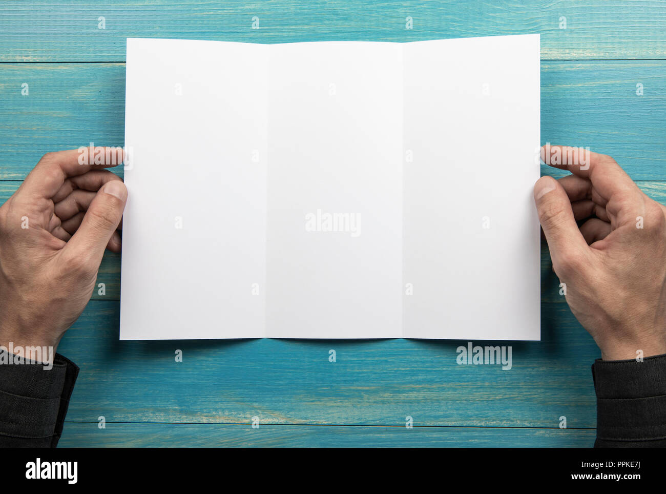Mens hands holding empty white booklet on blue wooden background. View ...