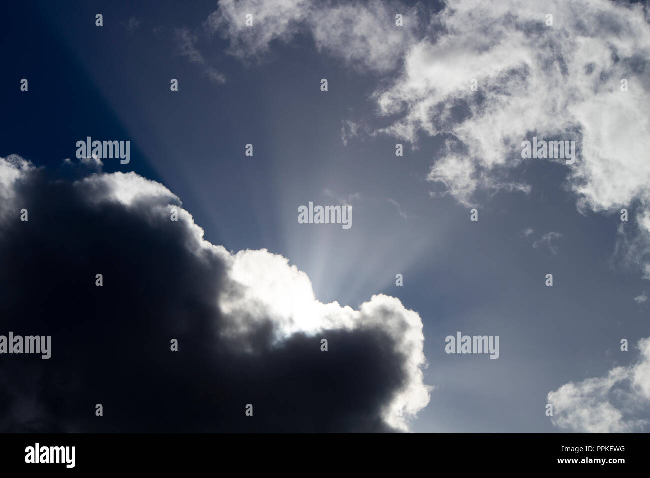 Sun disappearing behind rain clouds with rays of light extending ...