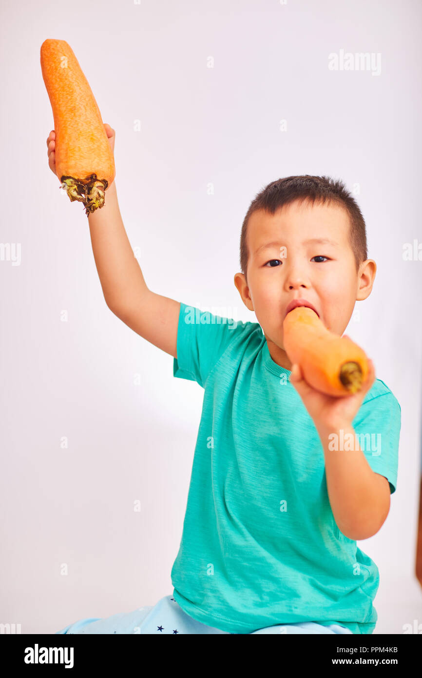 Child boy in a turquoise shirt, eating huge carrots, one carrot raised ...