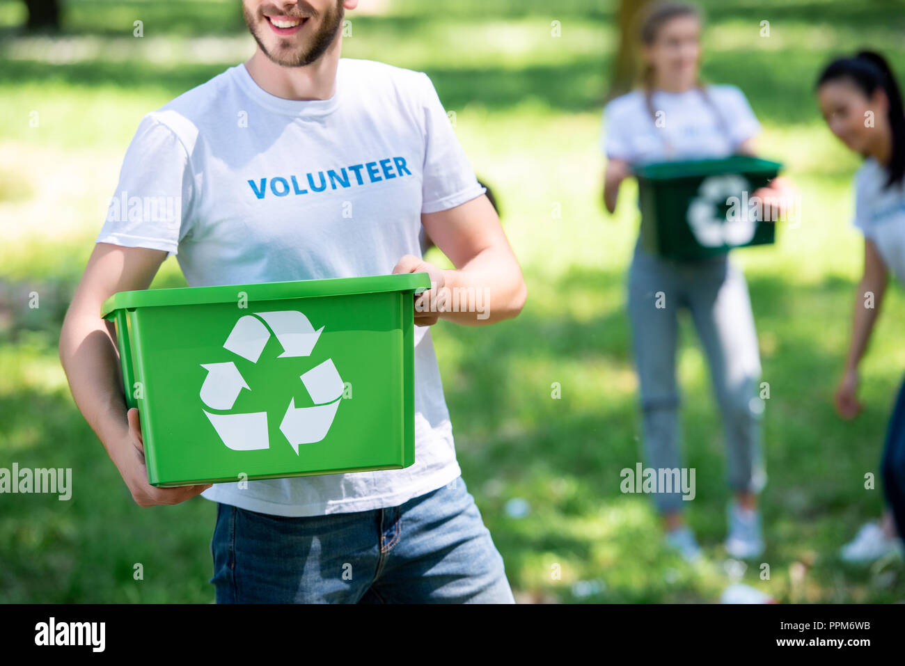 cropped view of volunteer holding green recycling box in park with ...
