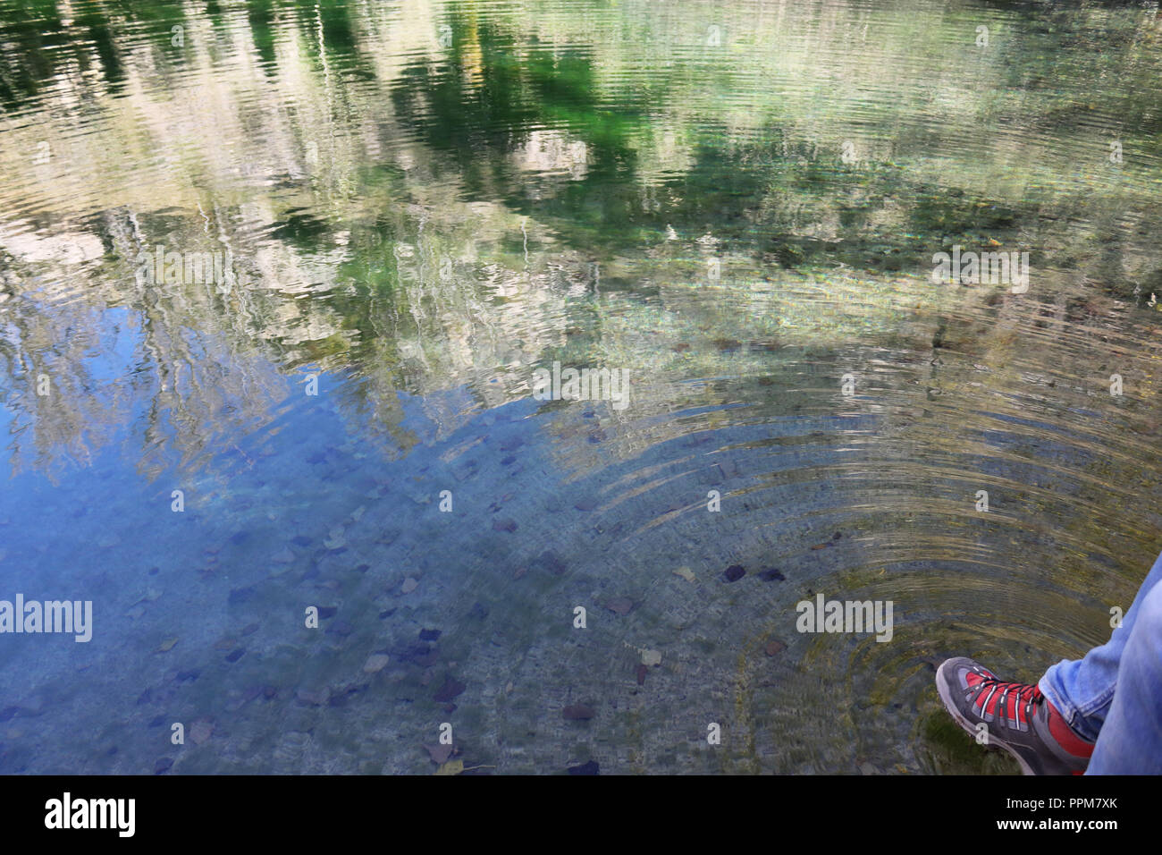 A man creating circular waves in a pond with mountains reflecting in it ...