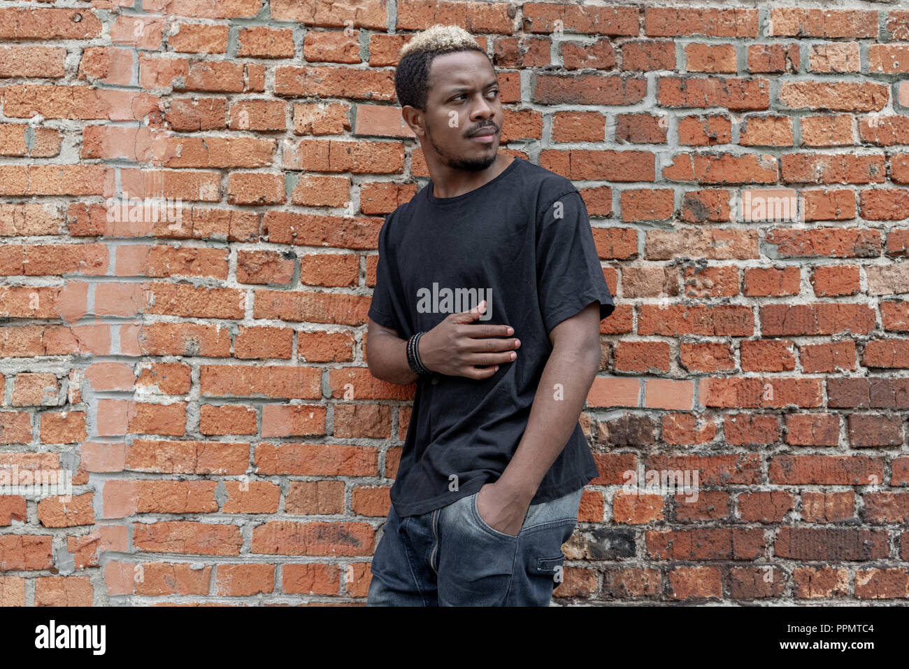Close up of dark-skinned man in black blank T-shirt on bricked ...