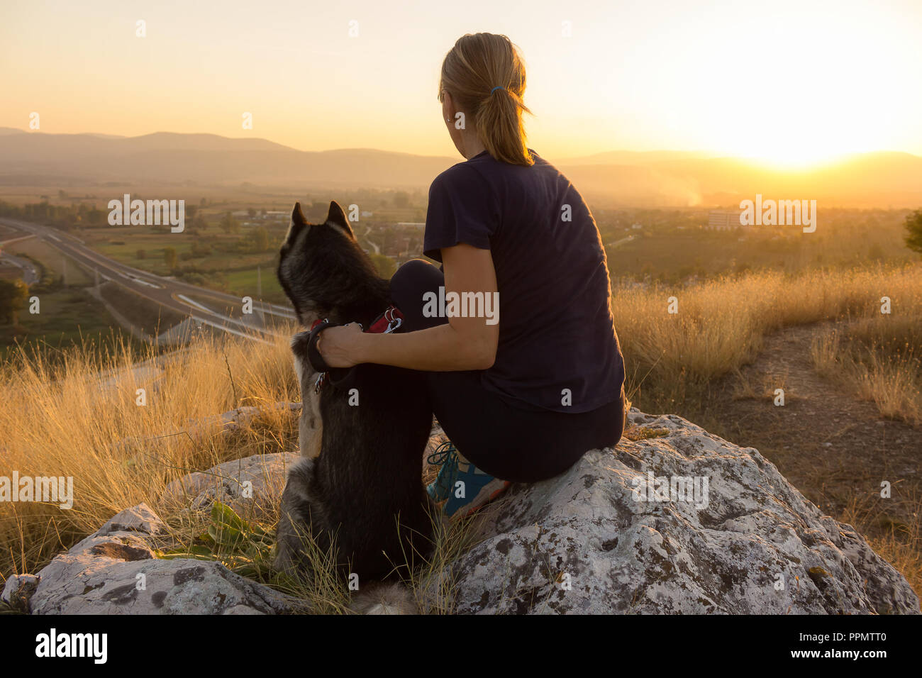 Woman and Siberian husky sitting on a rock and watching the sunset from ...