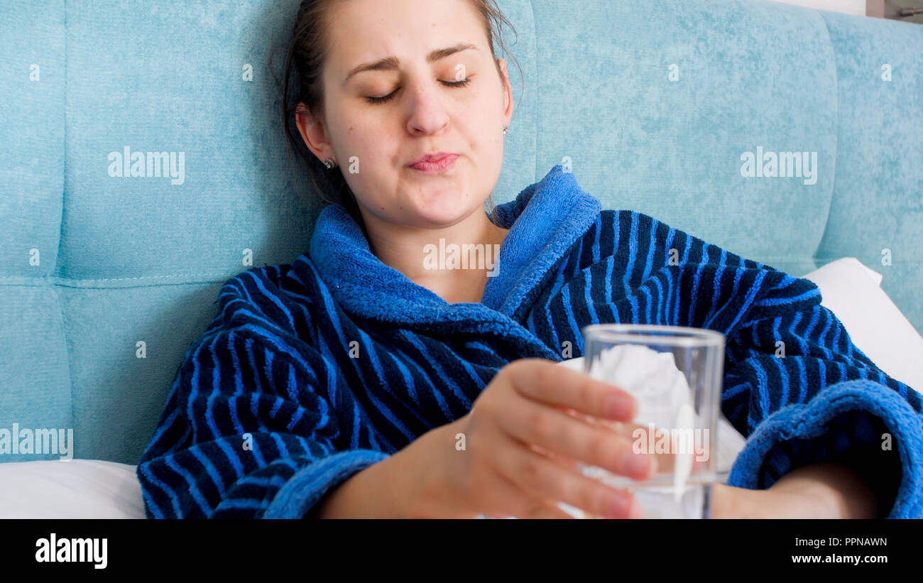 Portrait of sick young woman suffering from pain and holding glass of ...