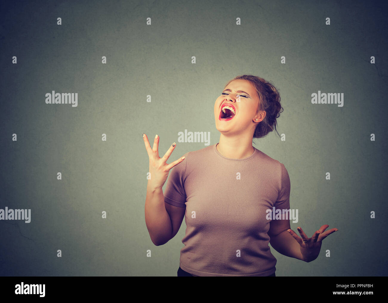 Young chunky woman screaming loudly in great hysteria on gray ...