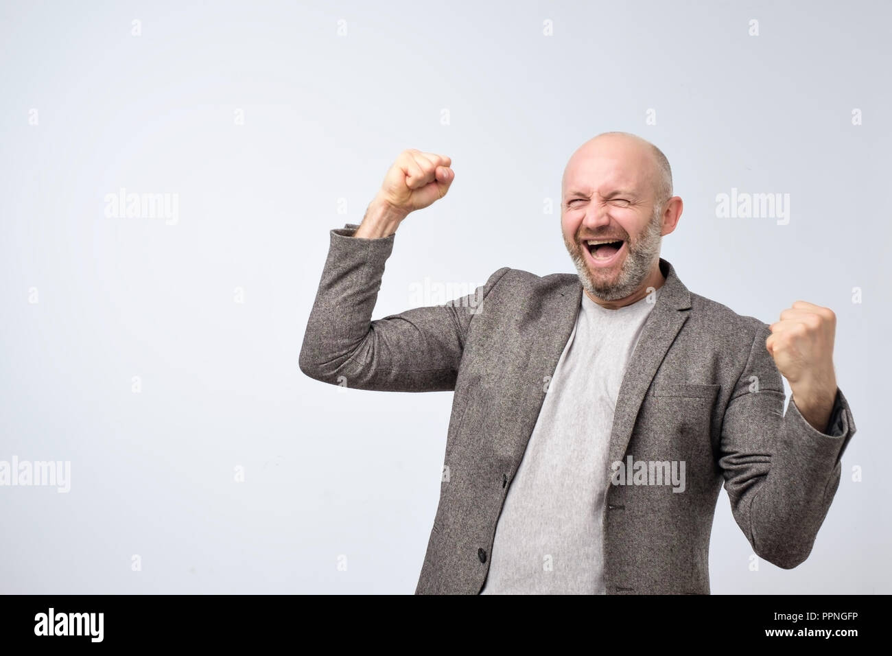Mature happy laughing man in suit with raised hands over gray ...