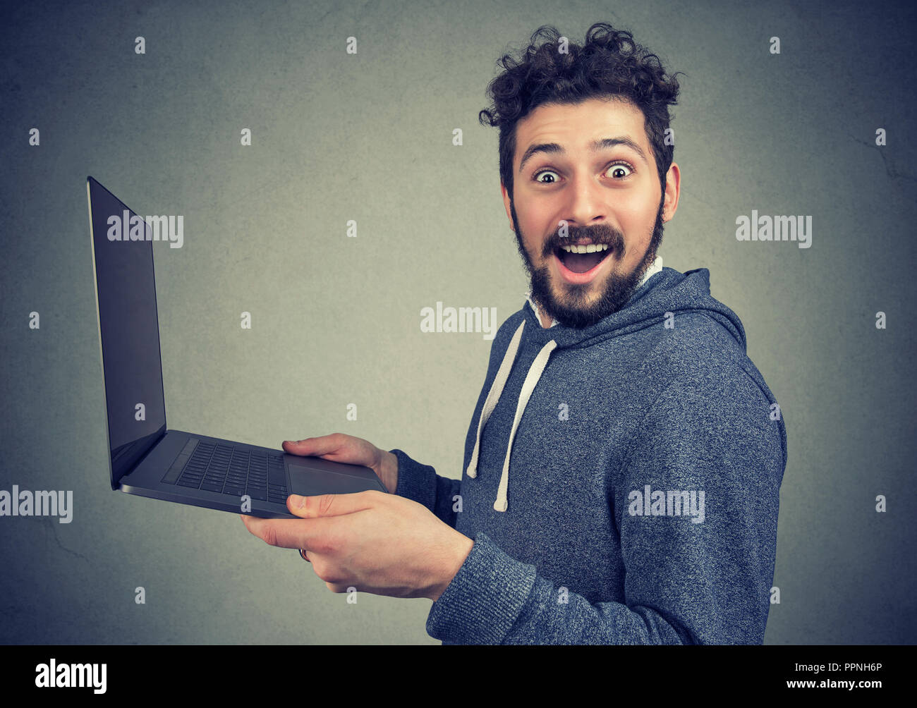 Surprised young man with laptop computer looking at camera in ...
