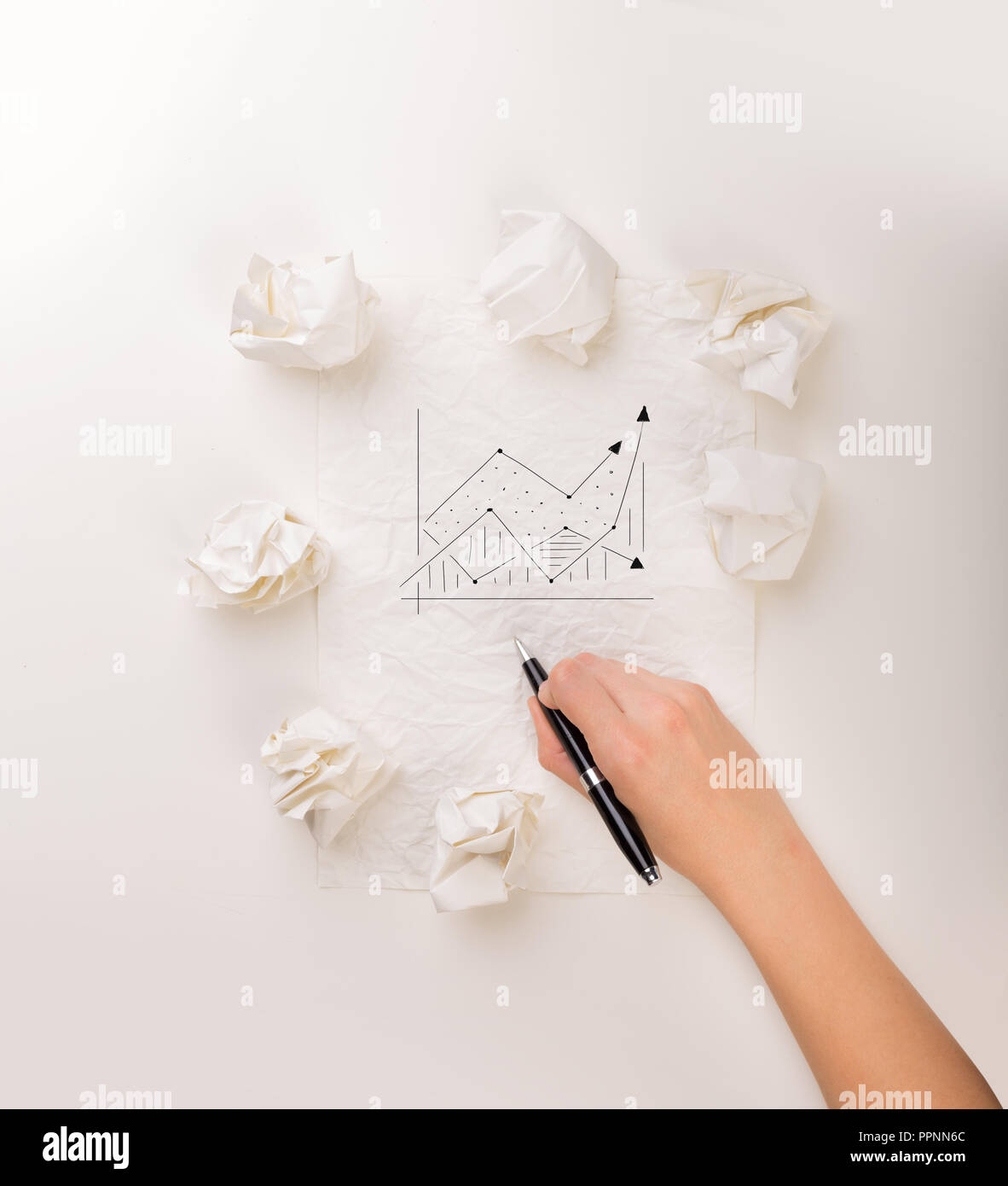 Female hand next to a few crumpled paper balls drawing a progress chart ...