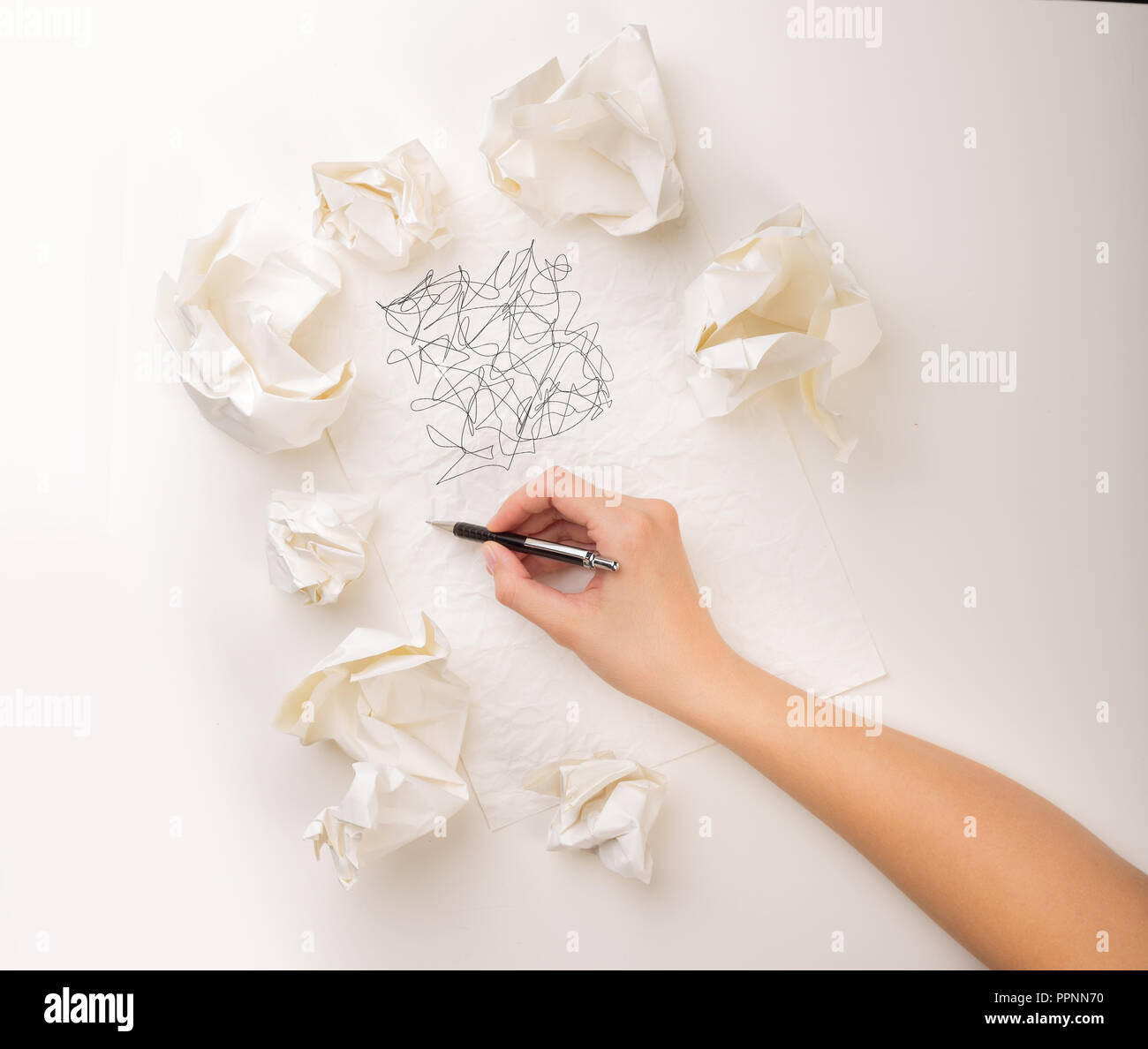 Female hand next to a few crumpled paper balls drawing random scribbles ...