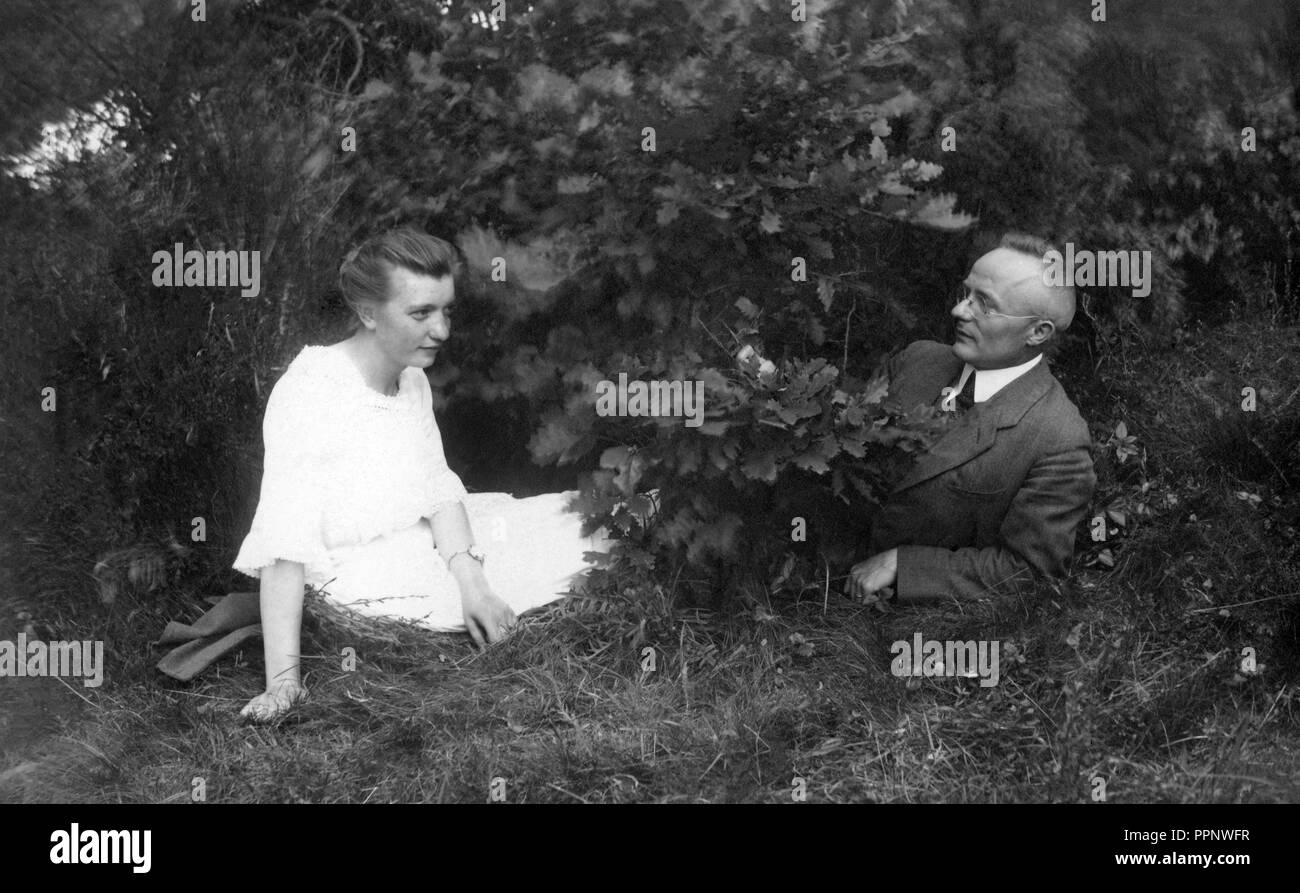 Couples, man and woman lie in a meadow hiding legs behind a bush, 1930s ...